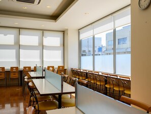 Sala de conferências com mesas, cadeiras, janelas amplas e um relógio na parede.