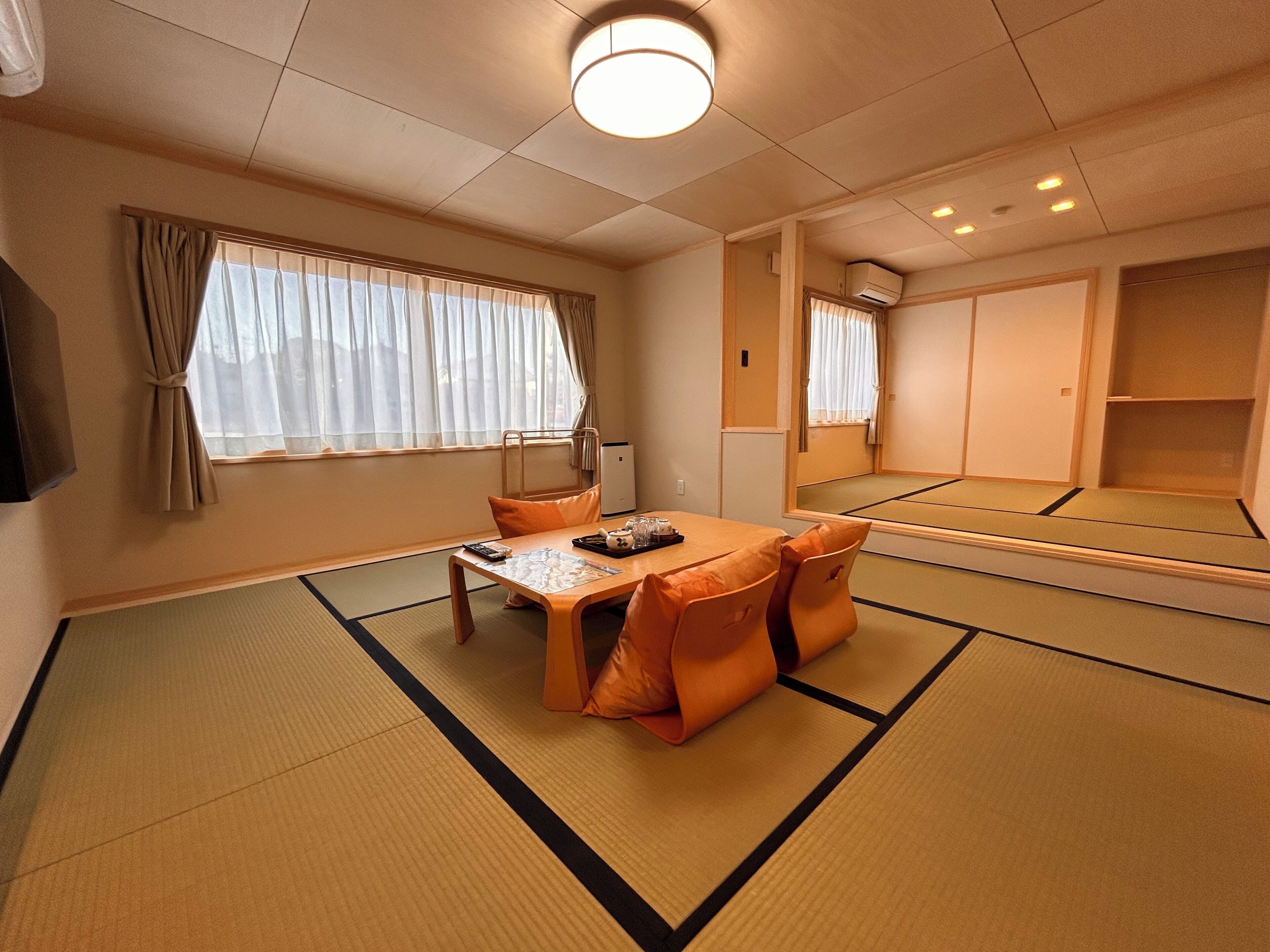 Um quarto tradicional japonês com tatames, uma mesa baixa, almofadas laranja, um espelho e uma luminária no teto.