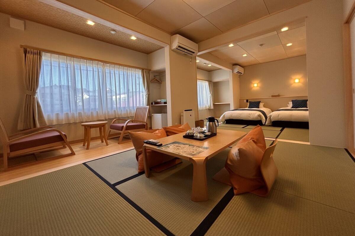Um quarto tradicional japonês com tatame, uma mesa baixa com almofadas, um sofá, uma cama e uma pequena mesa com chá.