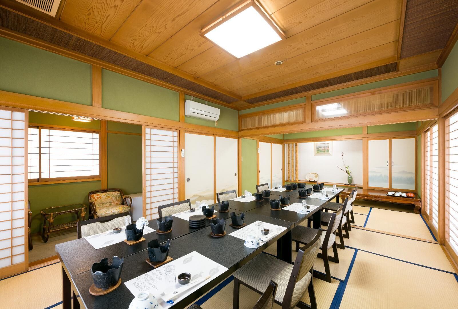 Quarto japonês tradicional com esteiras de tatame, uma mesa comprida com almofadas pretas e portas deslizantes.