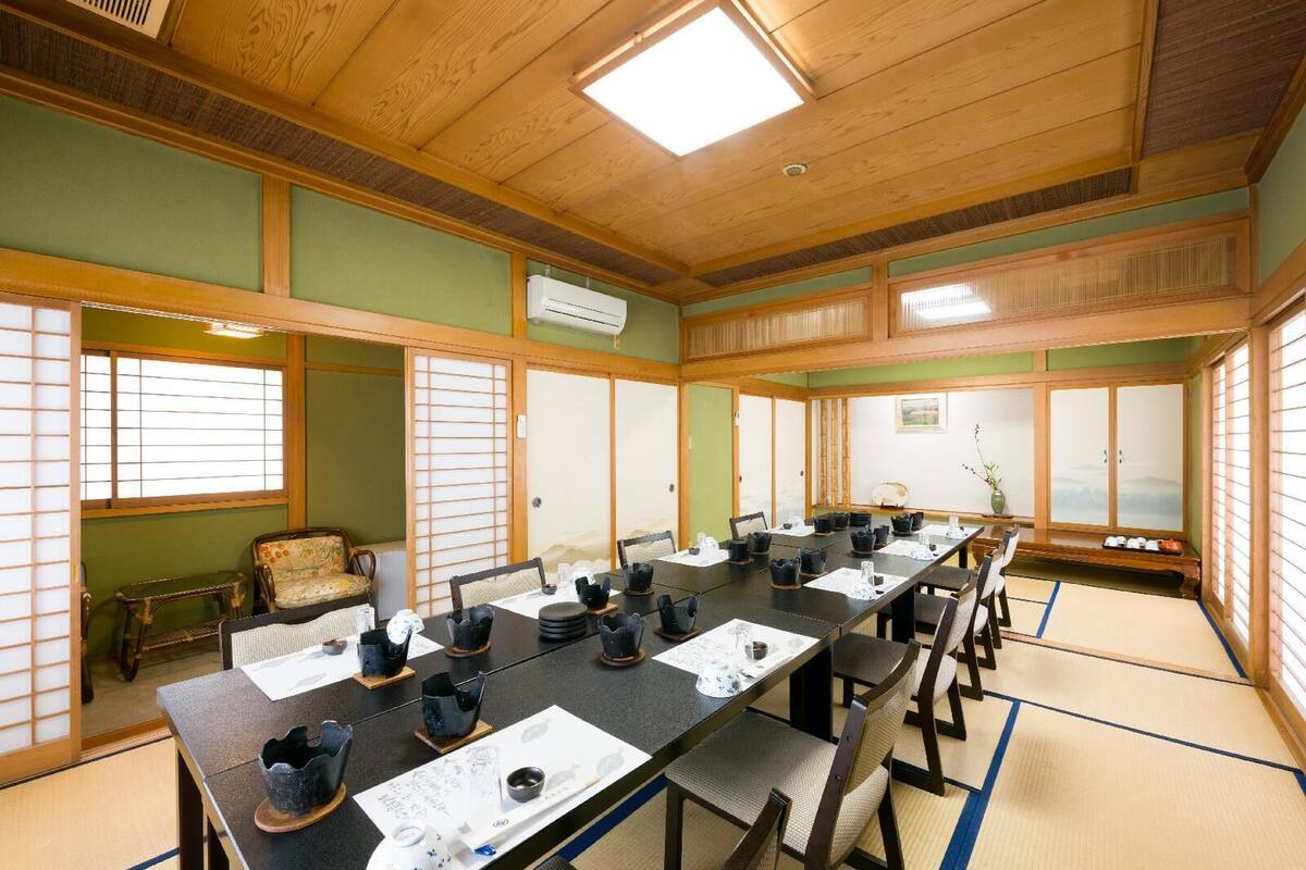 Quarto japonês tradicional com esteiras de tatame, uma mesa comprida com almofadas pretas e portas deslizantes.
