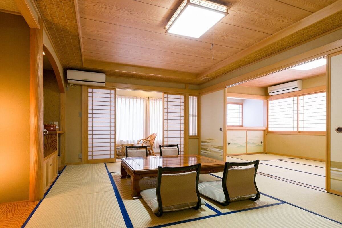 Um quarto japonês tradicional com tatames, uma mesa baixa com cadeiras, portas deslizantes e um ventilador de teto.