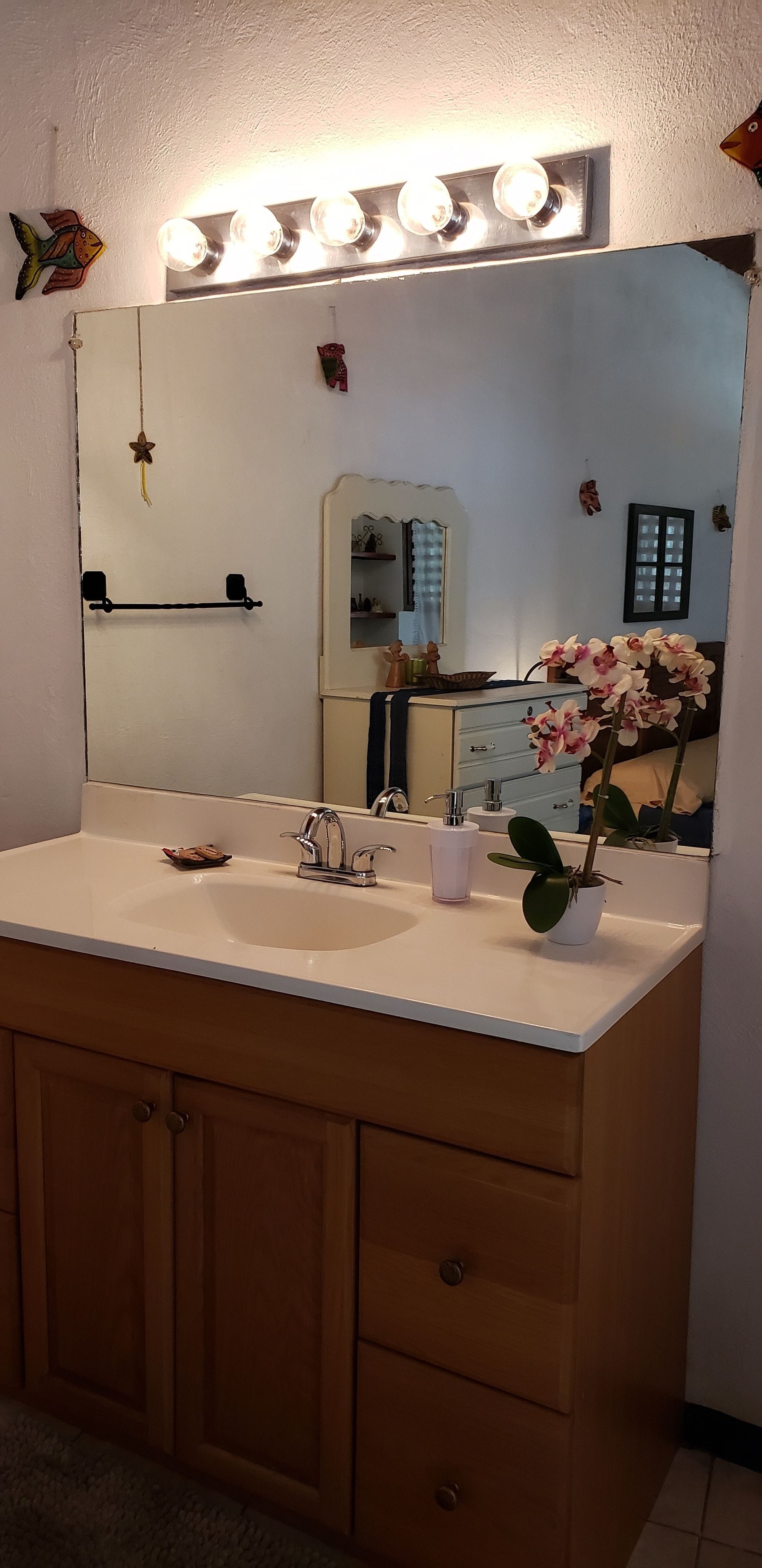 Casa de banho com lavatório, espelho e balcão. Há luzes sobre o espelho e uma prateleira com objetos decorativos.