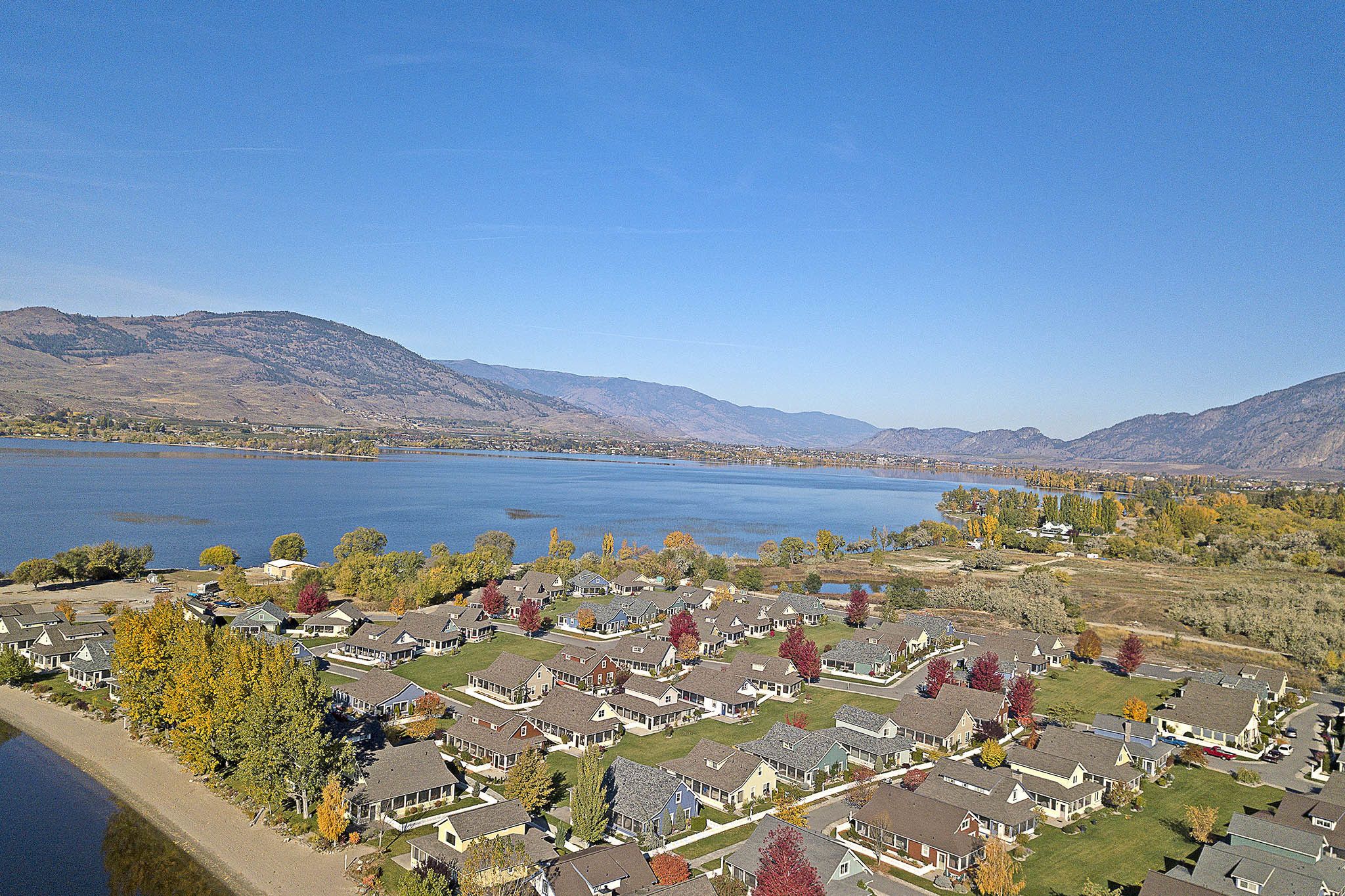 Zona residencial com casas perto de um lago, rodeada por montanhas.