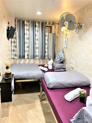 Quarto de hotel com duas camas, uma escrivaninha, um ventilador e área de chuveiro.