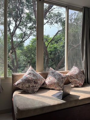 Um quarto com uma janela grande, um sofá com almofadas florais e um laptop sobre o sofá.