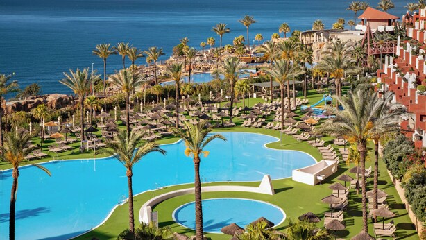 Um resort com uma piscina grande, palmeiras e vista para o oceano.