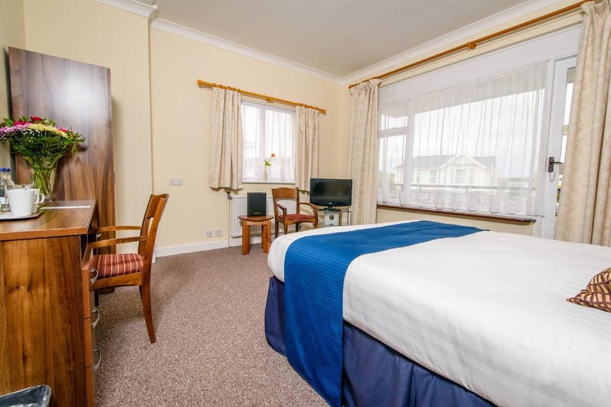 Quarto de hotel com uma cama grande, uma escrivaninha com cadeira, televisão e janela com cortinas.