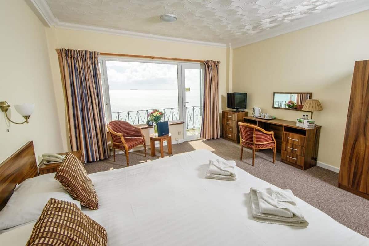 Quarto de hotel com cama, escrivaninha, televisão e varanda com cortinas.