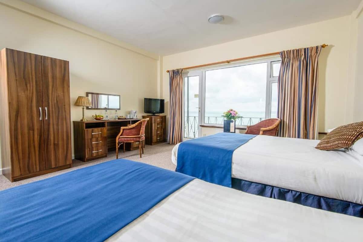 Quarto de hotel com duas camas, uma escrivaninha com televisão, um guarda-roupa e varanda com vista.