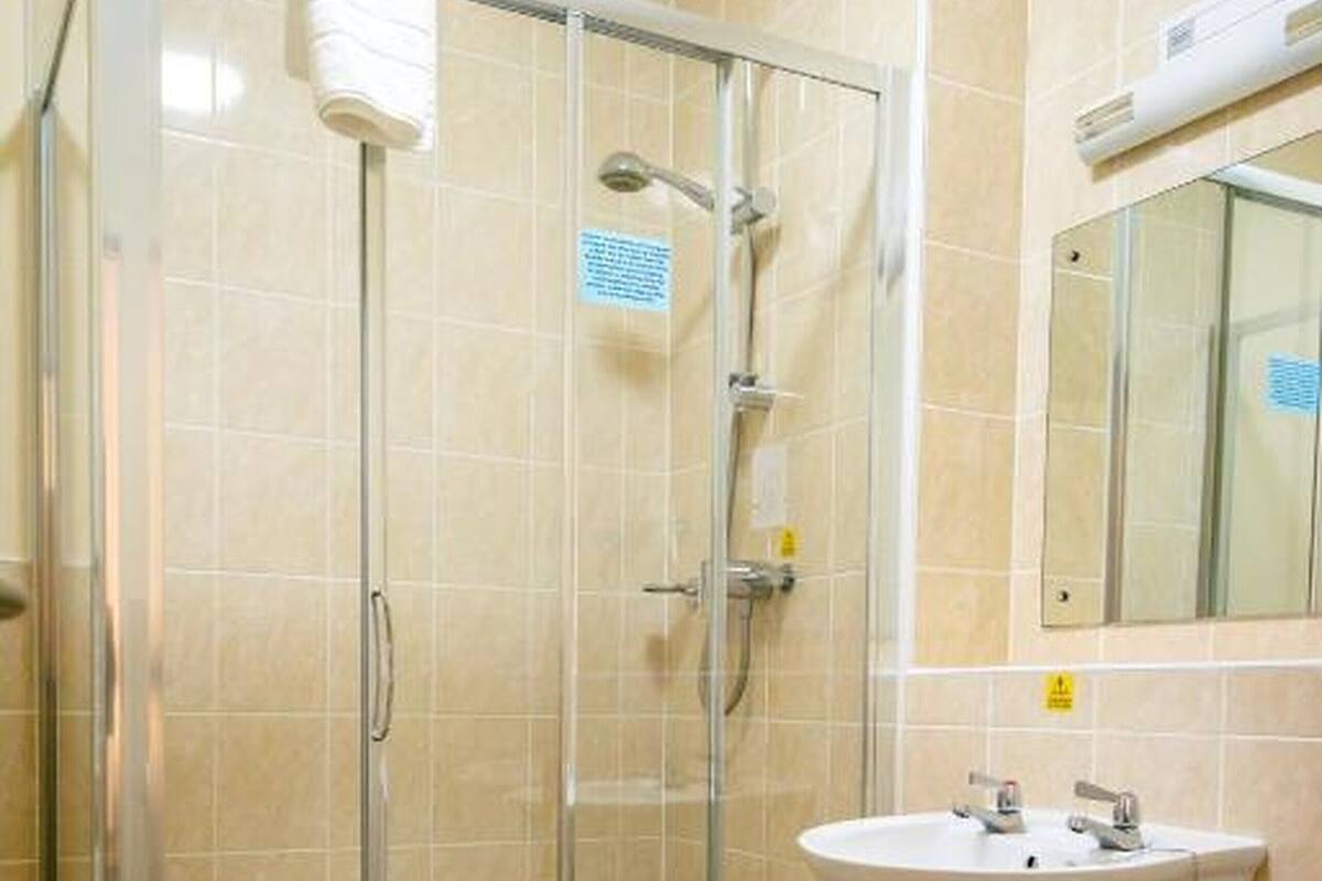 Uma casa de banho com cabine de duche em vidro, lavatório branco e espelho sobre o lavatório.
