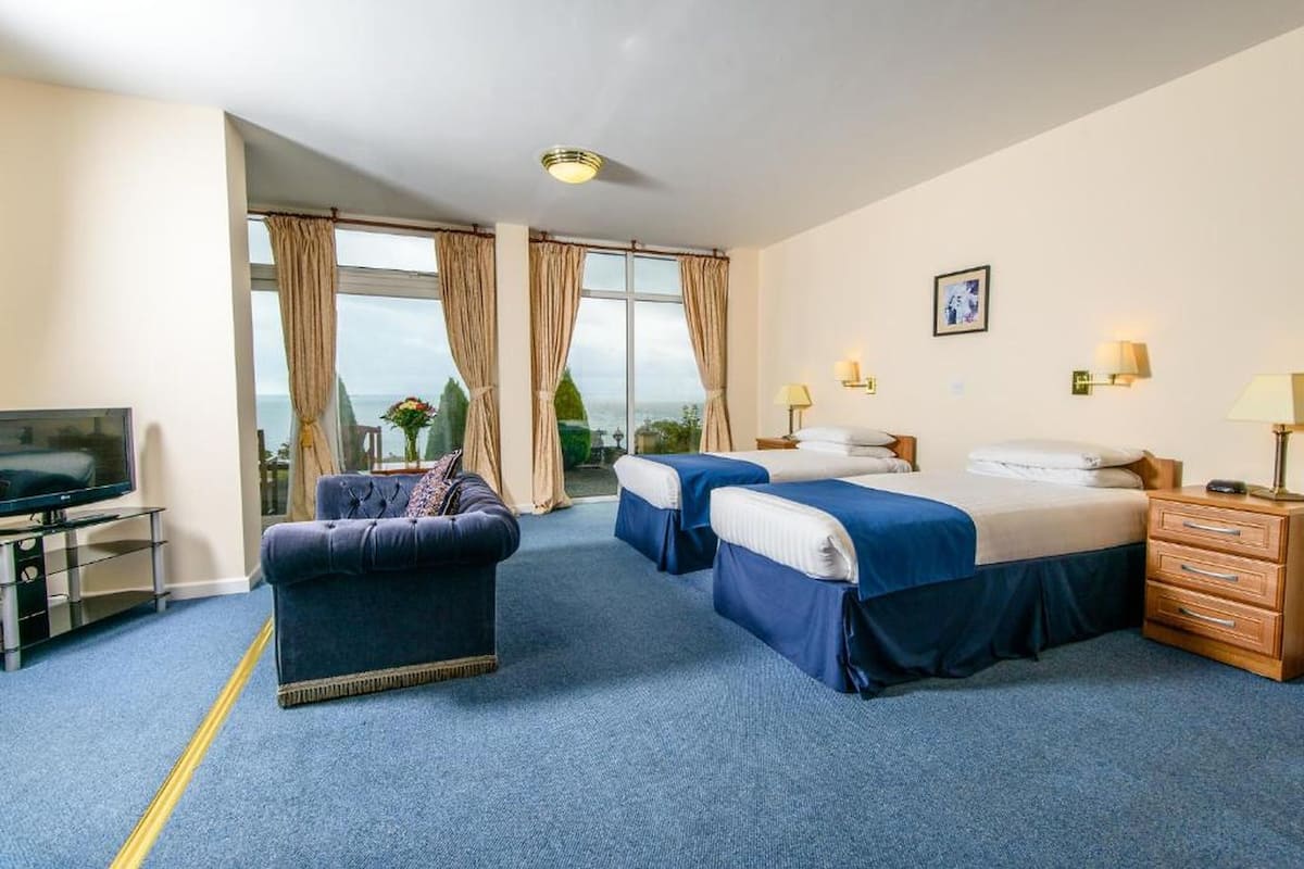 Quarto de hotel com duas camas, um sofá, uma televisão e varanda com vista.