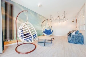 Uma sala de estar moderna com vista para o mar, apresentando uma cadeira suspensa, um sofá e uma mesa redonda.