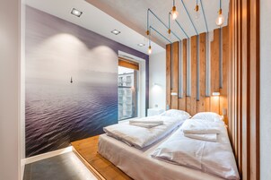 Quarto de hotel moderno com um mural grande de um mar calmo, cabeceira de madeira e cama com lençóis brancos.