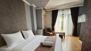Quarto de hotel com uma cama grande, uma cadeira, uma mesa pequena e uma televisão.