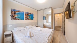 Quarto de hotel com uma cama grande, uma mesa de cabeceira e um espelho. Há duas pinturas na parede acima da cama.