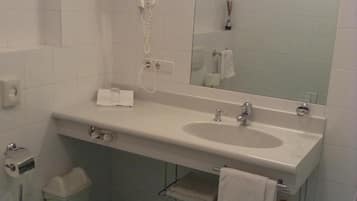 Casa de banho com lavatório branco, espelho, secador de cabelo e sanita.