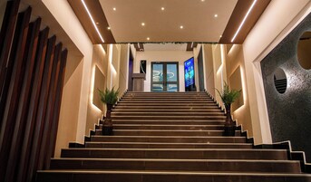 Escadaria com design moderno, levando a uma área de recepção com um painel digital e uma porta.