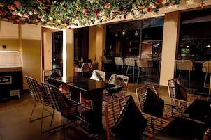Uma sala de jantar com uma mesa preta e cadeiras de vime, rodeada por paredes com grandes janelas.