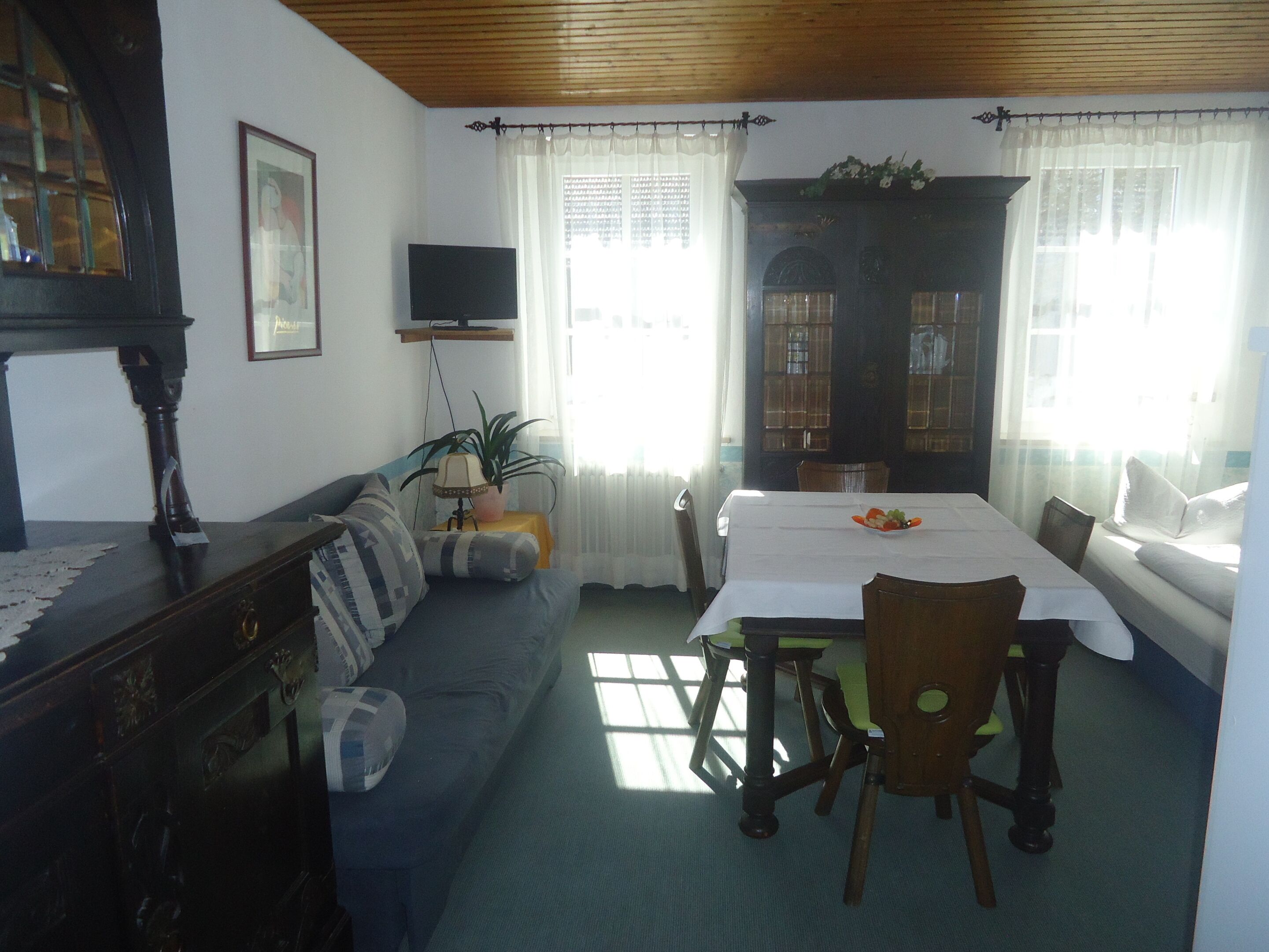 Uma área de refeições com uma mesa posta para dois, um sofá, uma televisão e uma janela com cortinas.