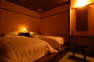 Quarto com duas camas, uma mesa de cabeceira, uma pequena mesa e um banco de madeira.