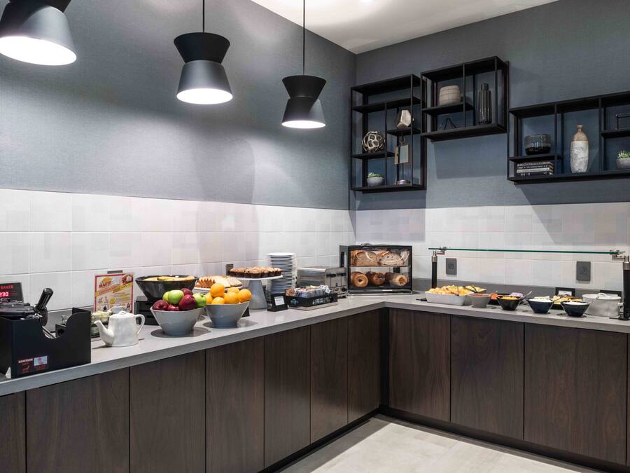 Uma cozinha moderna com bancada para refeições, cafeteira e diversas opções de alimentos.