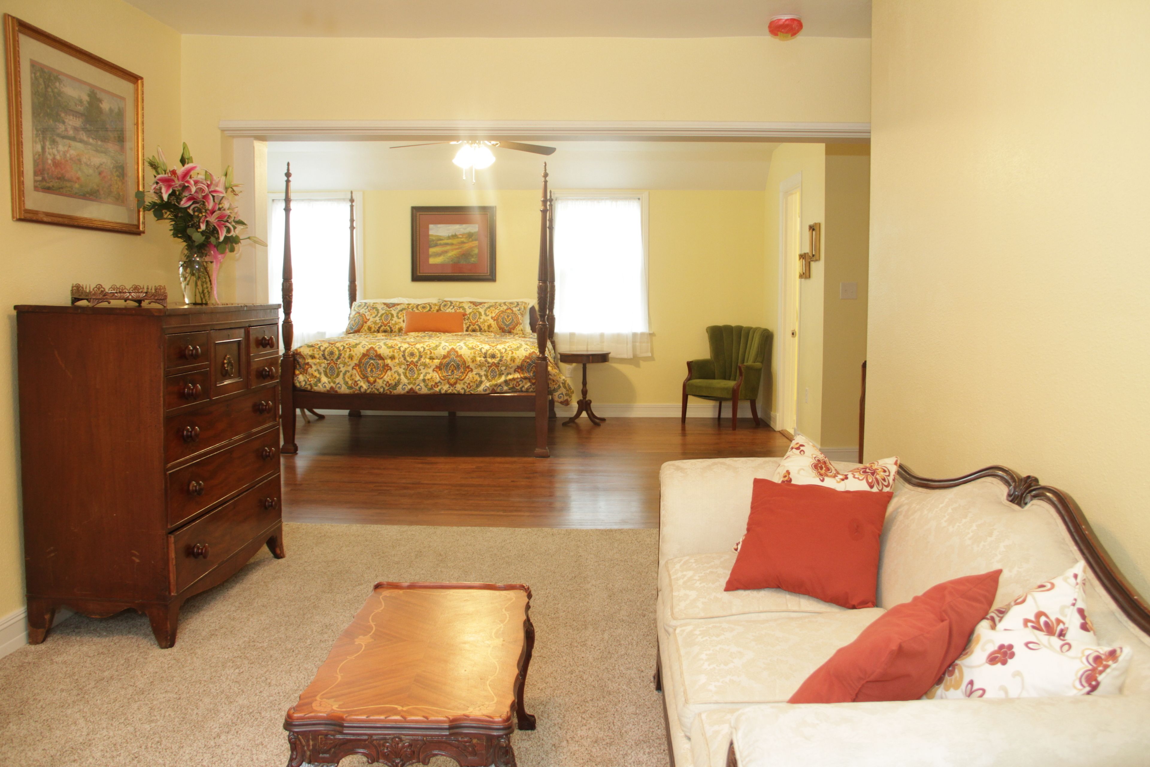 Quarto com cama de dossel, cómoda de madeira, cadeira verde e sofá branco com almofadas vermelhas.