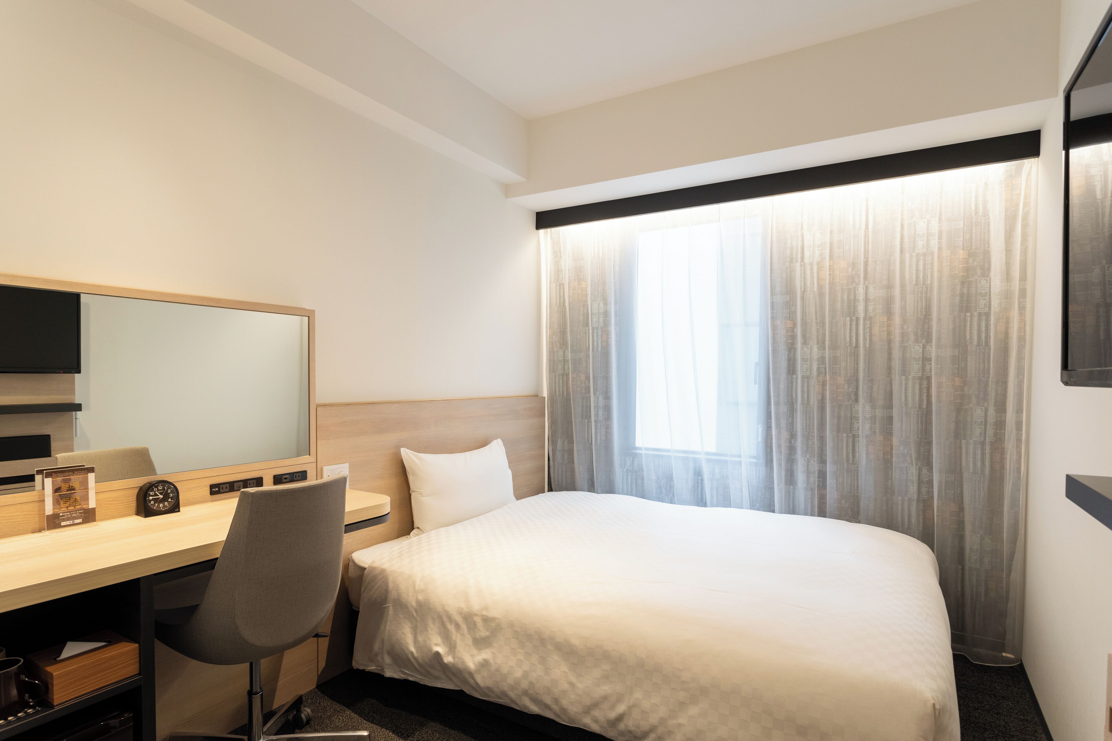 Quarto de hotel com cama, escrivaninha e cadeira, televisão de tela plana, mesa de cabeceira e janela com cortinas.