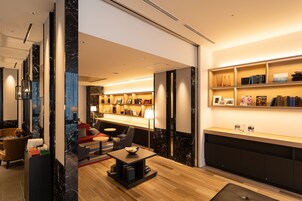 Um hall de hotel moderno com uma receção de mármore, área de estar e uma estante com revistas e livros.