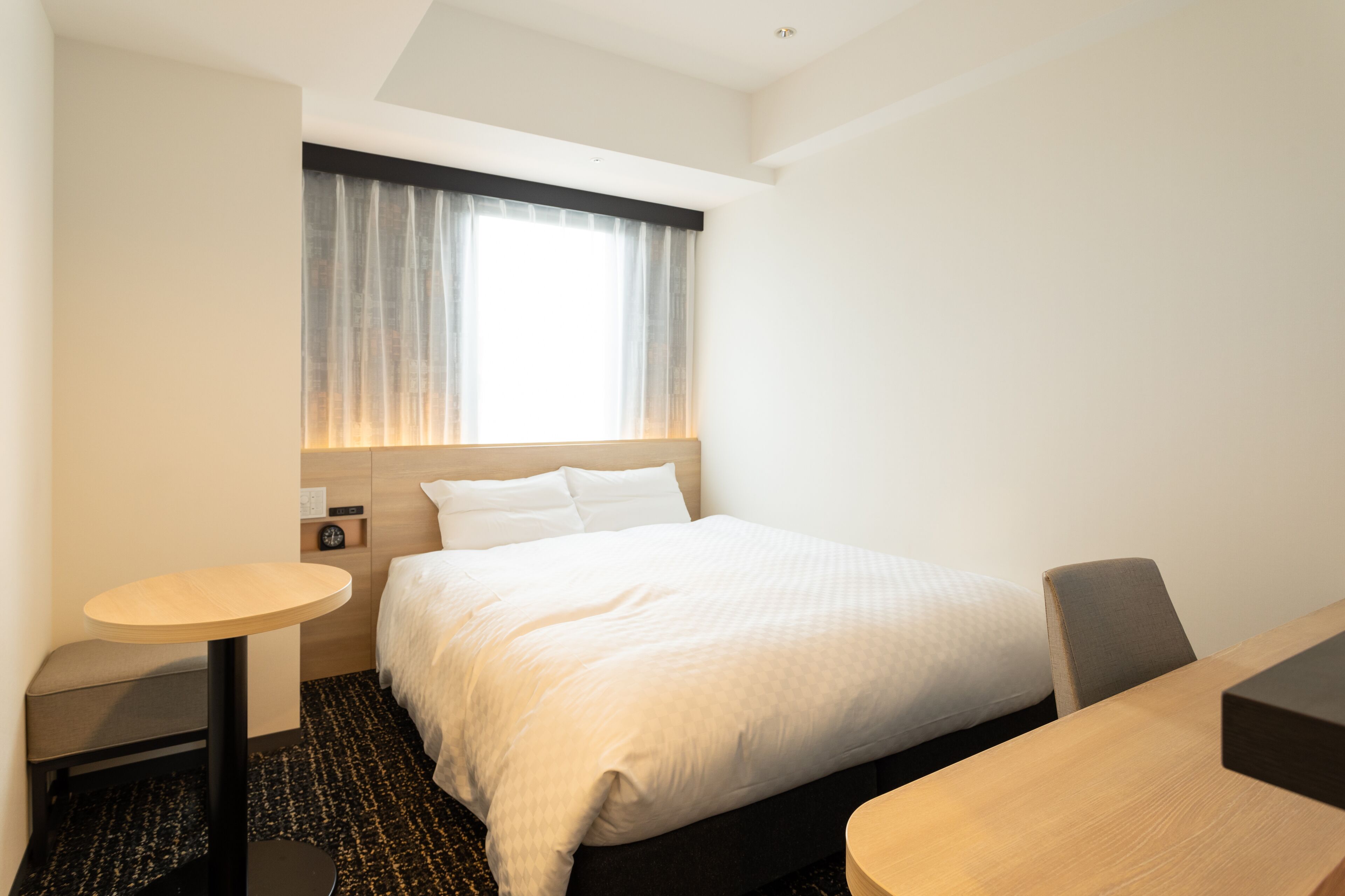 Quarto de hotel com cama, mesa redonda, cadeira e escrivaninha.