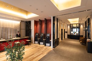 Um hall de hotel moderno com balcão de recepção, totens de autoatendimento, área de recepção e sala de estar com planta.