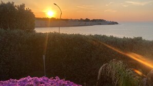Vista do pôr do sol com um corpo d'água, um poste de luz e vegetação em primeiro plano.