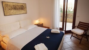 Quarto com cama, mesa de cabeceira, cadeira, quadro e porta de vidro corrediça para o exterior.