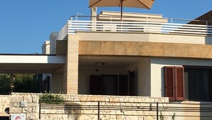 Um edifício moderno com fachada de pedra, uma varanda com guarda-sol bege e uma placa indicando um hotel.