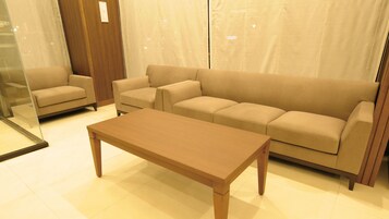 Sala de estar com sofá bege, mesa de centro de madeira e divisória de vidro.