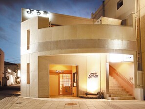 Um edifício de dois andares com entrada visível e escadaria que dá acesso a um andar superior.