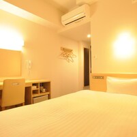 Quarto de hotel com cama, escrivaninha, cadeira, guarda-roupa e ar condicionado.