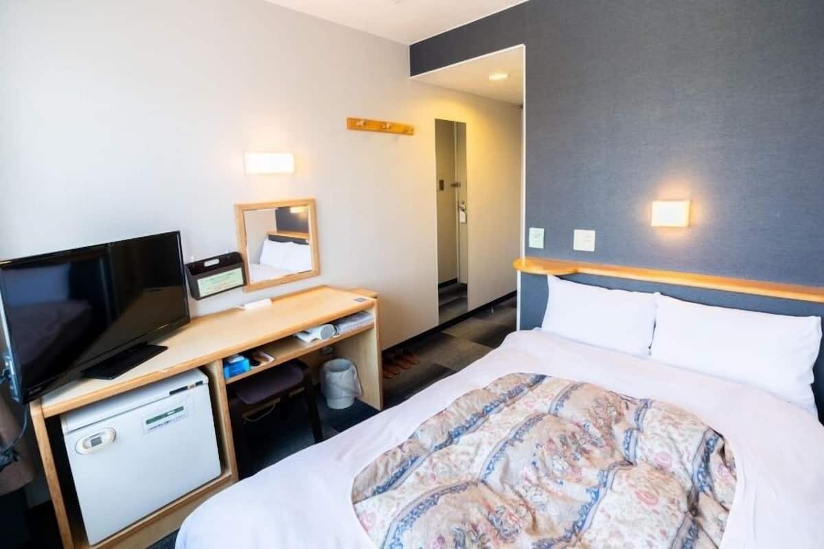 Quarto de hotel com uma cama, uma secretária com televisão, um espelho e um pequeno armário.
