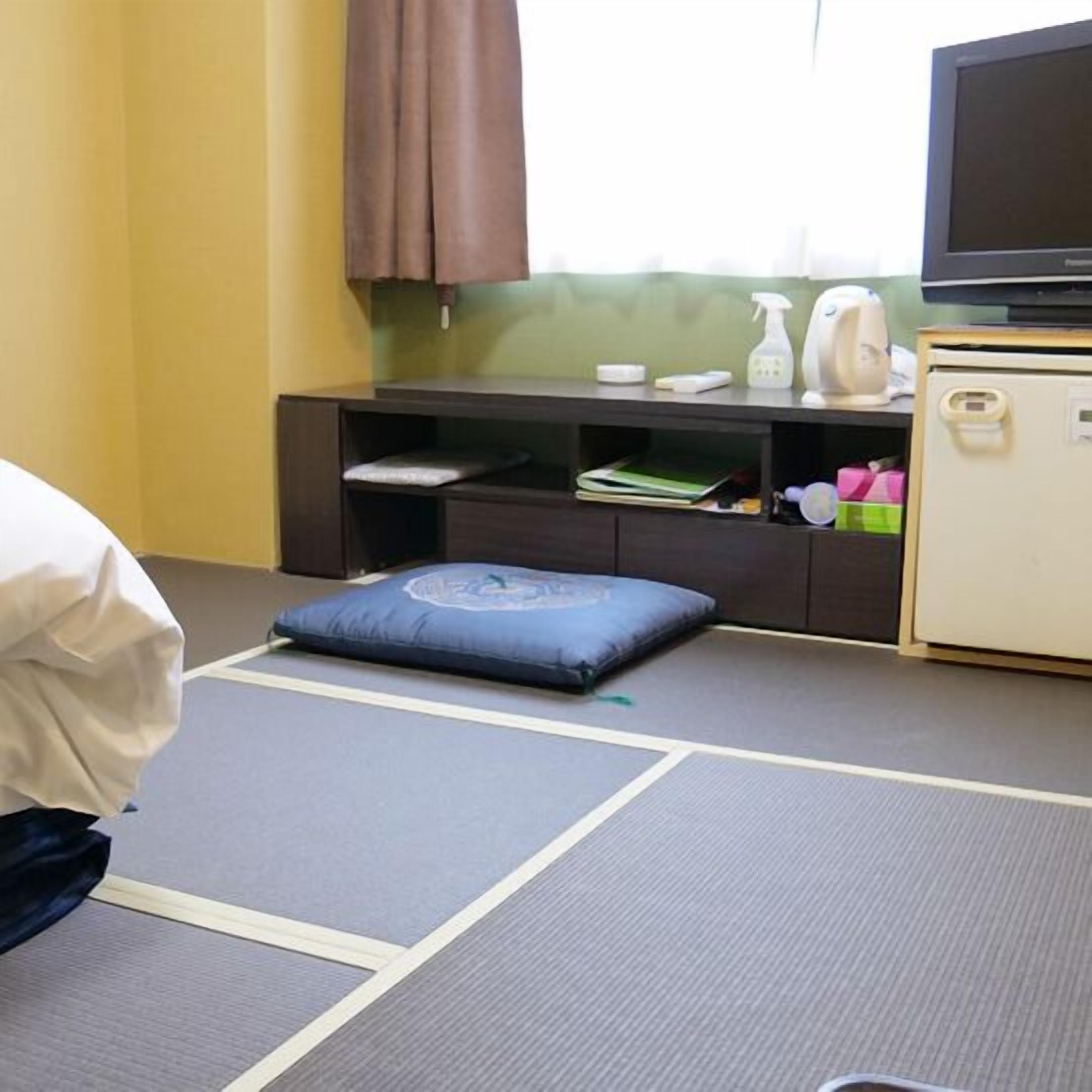 Quarto de hotel com cama, um pequeno sofá, escrivaninha com computador, televisão e armário com diversos objetos.