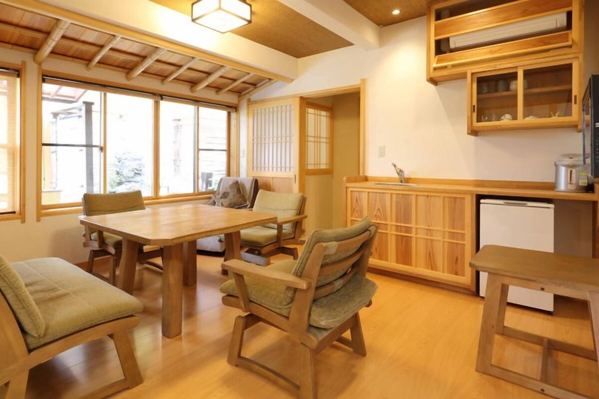 Quarto japonês tradicional com chão de esteiras de tatame, uma mesa de jantar de madeira e uma cozinha com frigorífico e armários.
