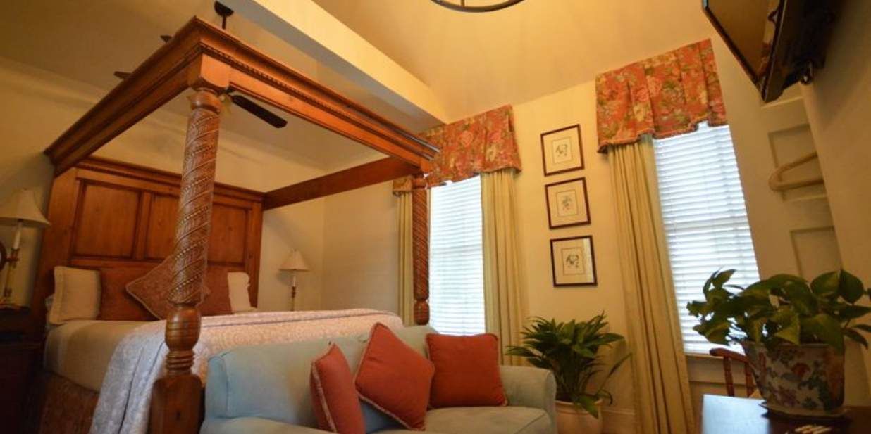Quarto com cama de dossel, sofá, planta em vaso e janela com cortinas.