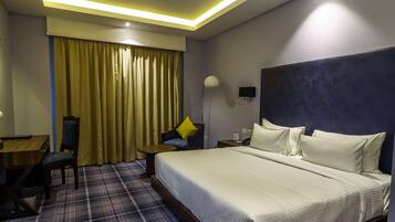 Quarto de hotel com cama, escrivaninha, cadeira, mesa pequena e luminária.