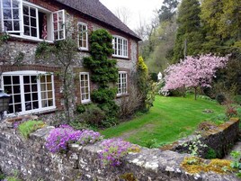 Uma casa de pedra com um jardim bem cuidado, incluindo gramado e plantas floridas.