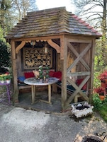 Um gazebo de madeira com telhado de cerâmica, um banco e uma mesa com vasos de plantas.