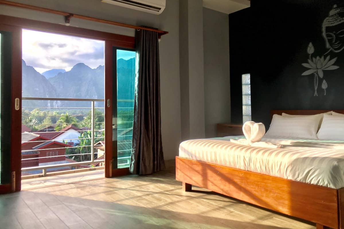 Quarto com uma cama grande, vista para montanhas por uma porta de correr e um ventilador de teto.