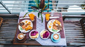Mesa posta para o café da manhã, com ovos, torradas e frutas, com vista para uma piscina ao fundo.