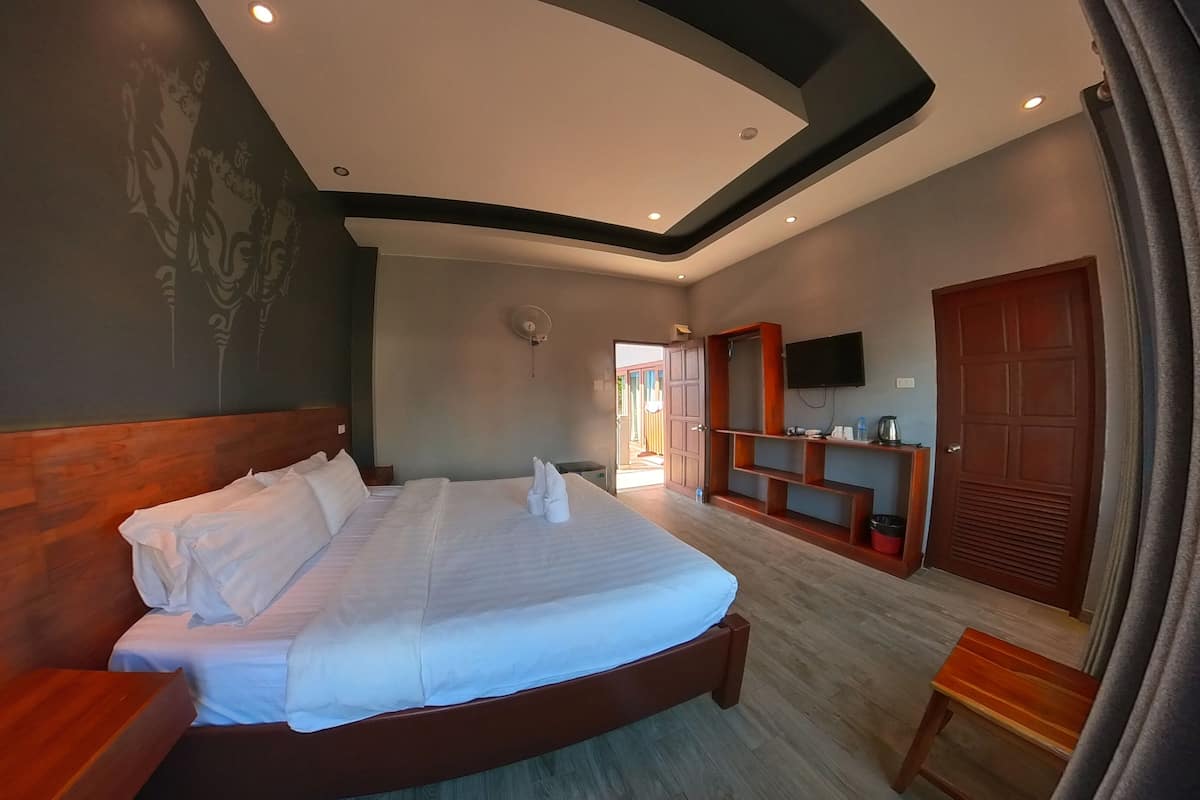 Quarto de hotel moderno com uma cama grande, cabeceira de madeira, uma televisão de tela plana e uma pequena mesa de madeira.