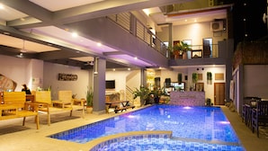 Piscina interior em vários níveis com azulejos de mosaico azul, assentos de madeira e uma escada conectando os níveis.