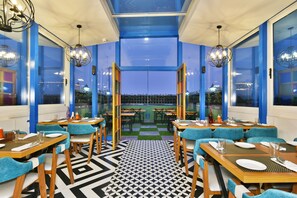 Restaurante com paredes azuis, mesas de madeira e cadeiras verde-água.