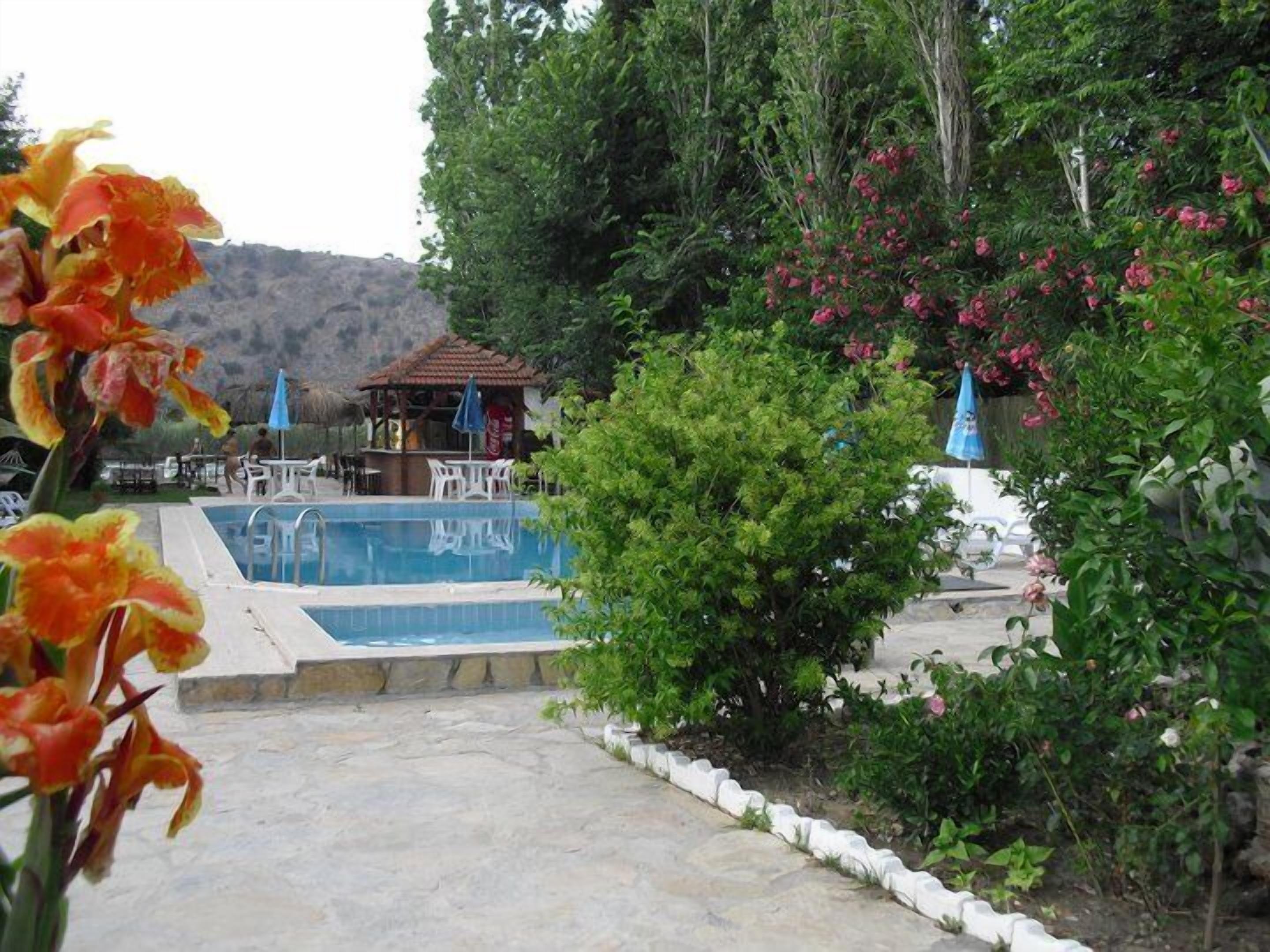 Área de piscina com um pequeno gazebo, rodeada por vegetação exuberante e plantas floridas.